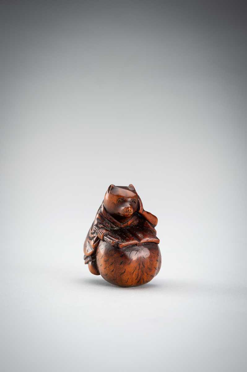Lot 499 - AN AMUSING WOOD NETSUKE OF A TANUKI READING