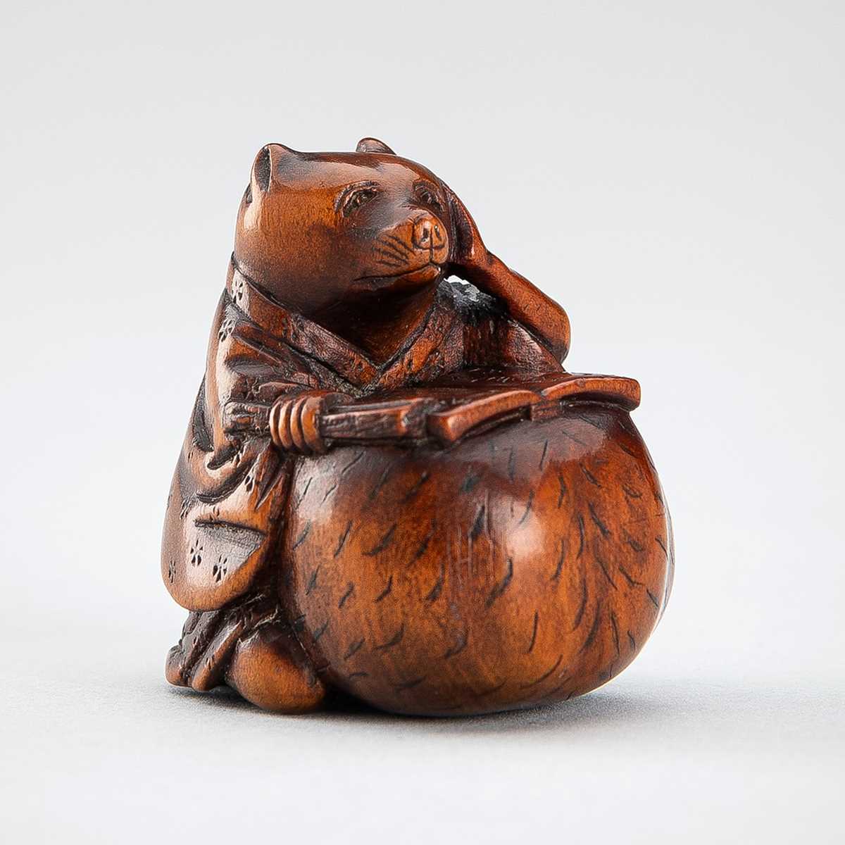 Lot 499 - AN AMUSING WOOD NETSUKE OF A TANUKI READING
