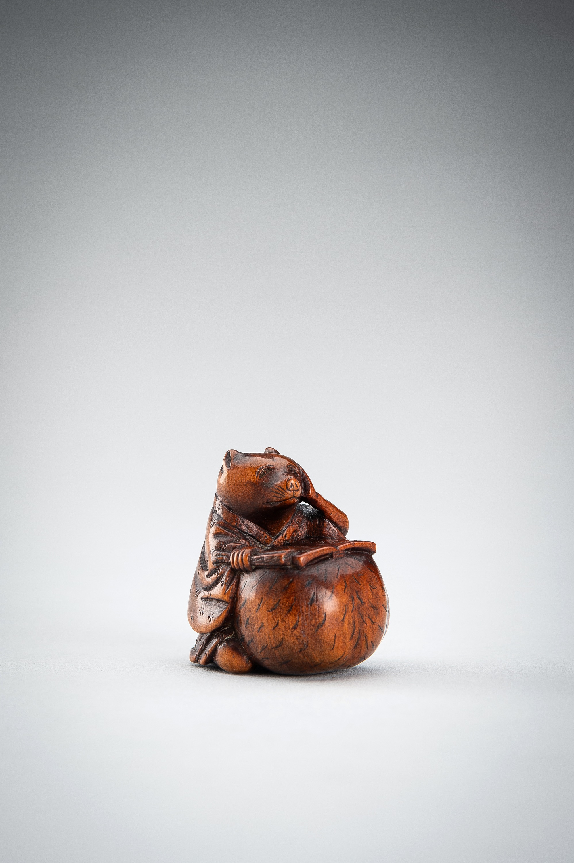 Lot 499 - AN AMUSING WOOD NETSUKE OF A TANUKI READING
