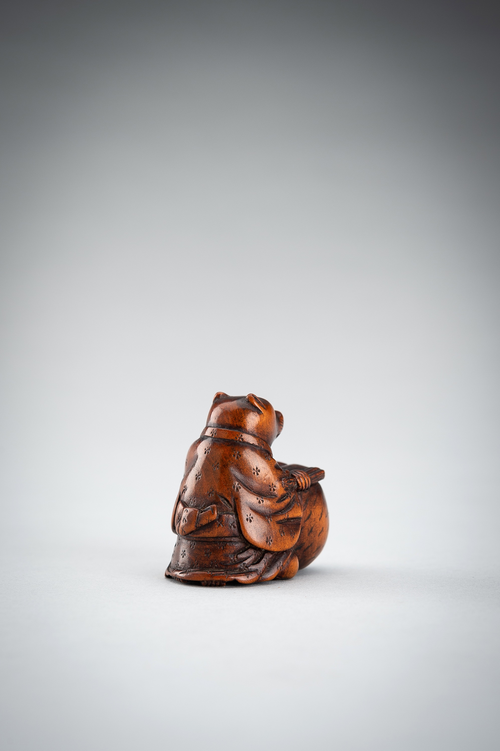 Lot 499 - AN AMUSING WOOD NETSUKE OF A TANUKI READING