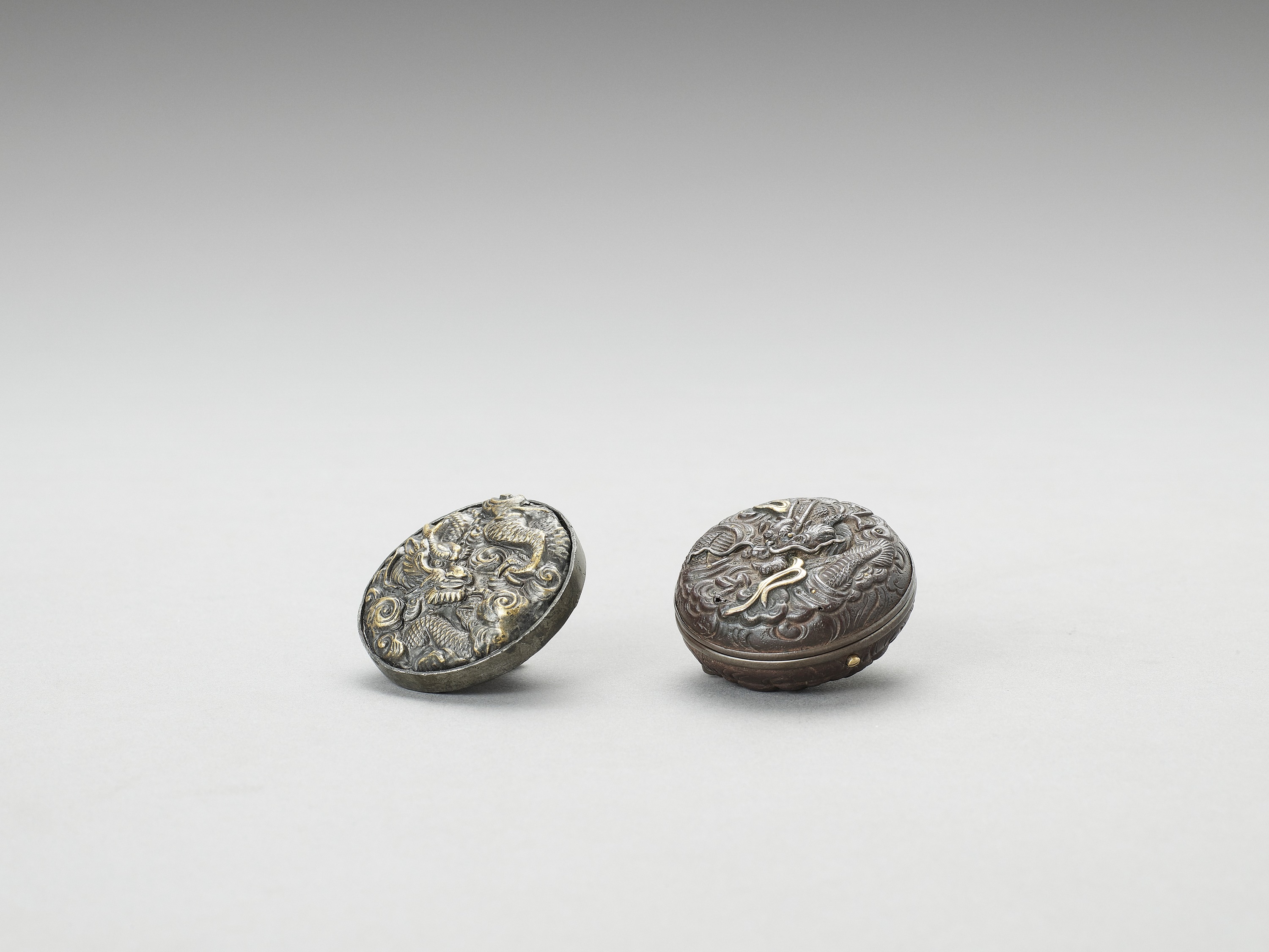 Lot 334 - TWO PARCEL-GILT METAL MANJU NETSUKE WITH