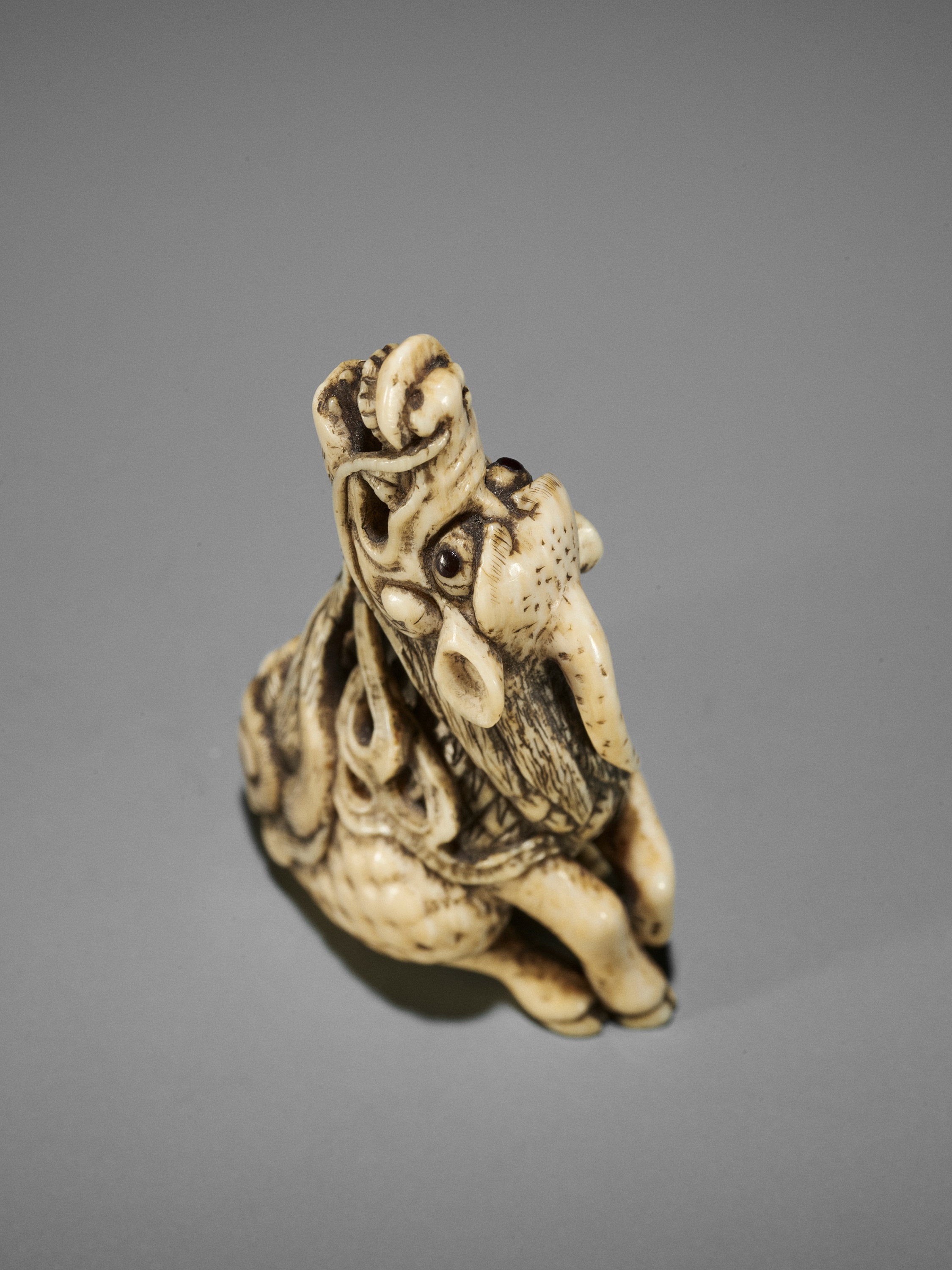 Lot 191 - AN IVORY NETSUKE OF A BAYING KIRIN IN THE